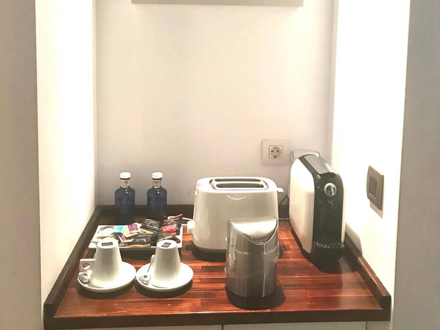 Uma pequena cozinha compacta com torradeira, chaleira e cafeteira em bancada de madeira.