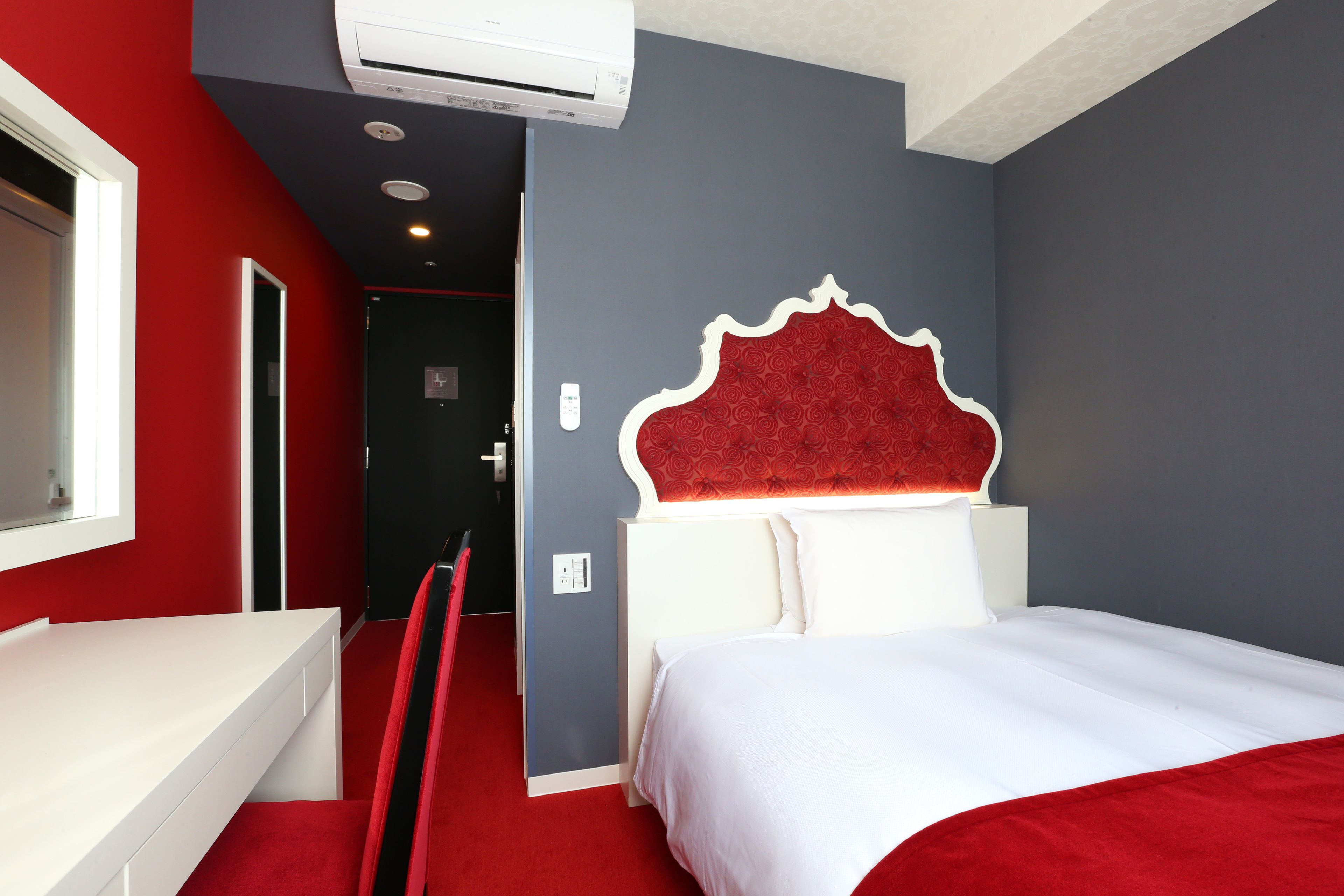 Quarto de hotel com esquema de cores vermelho e cinza, cama branca e parede de destaque vermelha.