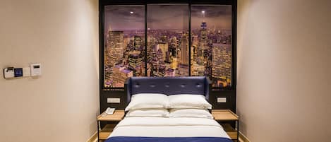 Quarto de hotel com uma cama grande, uma mesa de cabeceira, um telefone e vista para a cidade.