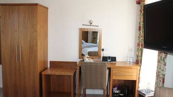Quarto de hotel com guarda-roupa de madeira, escrivaninha com cadeira, espelho, televisão e um pequeno armário.