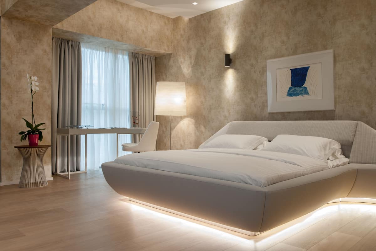 Quarto moderno com uma cama grande, uma escrivaninha, uma cadeira, um abajur e um vaso de planta.