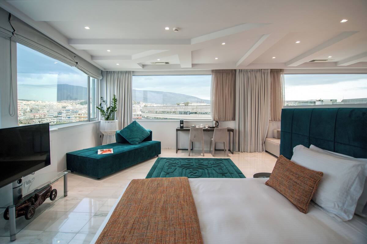Quarto de hotel moderno com uma cama grande, um sofá, uma escrivaninha e uma televisão.