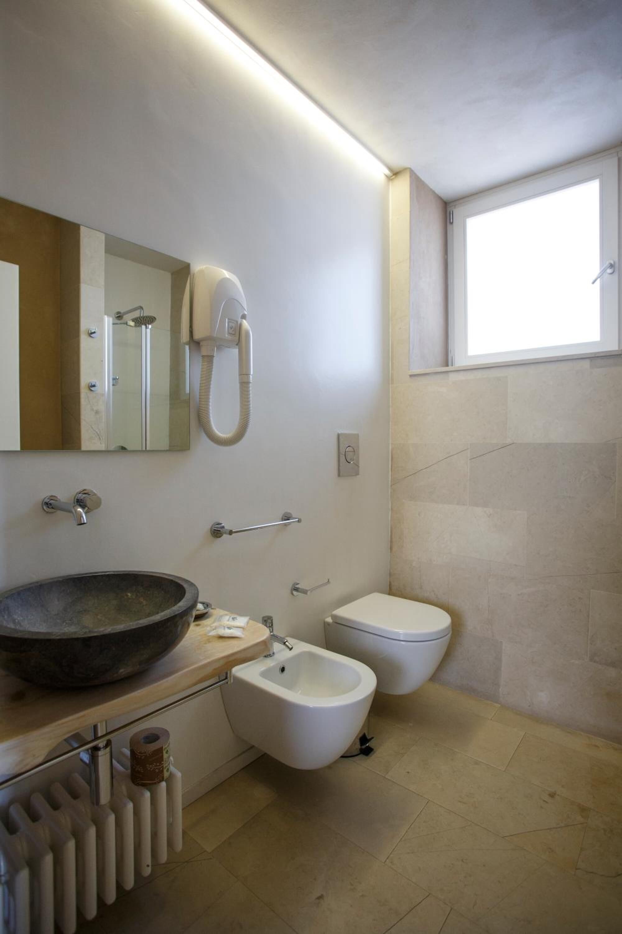 Uma casa de banho moderna com uma grande bacia, duas sanitas, um bidé, um porta-toalhas e uma janela que permite a entrada de luz natural.