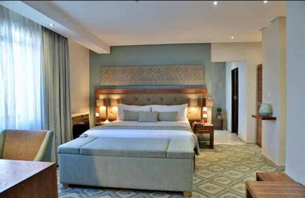Quarto de hotel com uma cama grande, mesas de cabeceira, uma escrivaninha e uma cadeira.