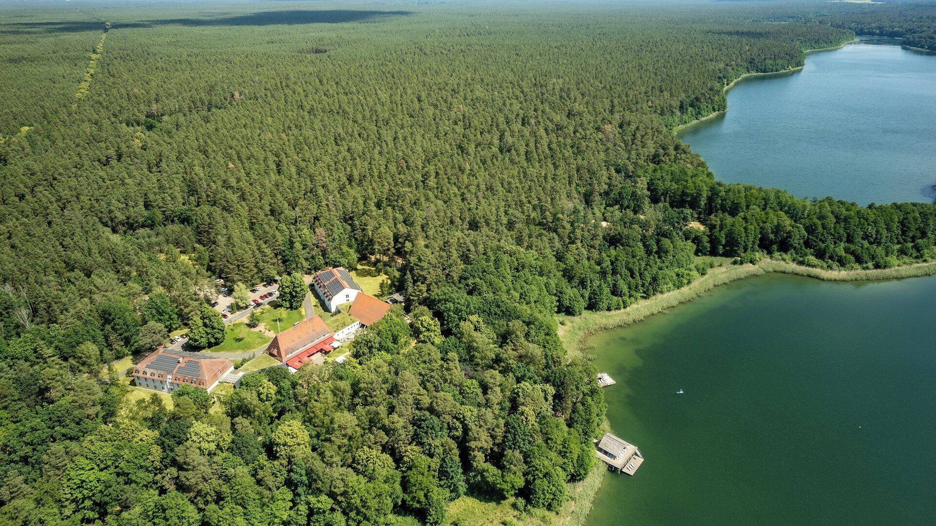 Vista aérea de uma área arborizada com um lago, um pequeno píer e um edifício com telhado vermelho.