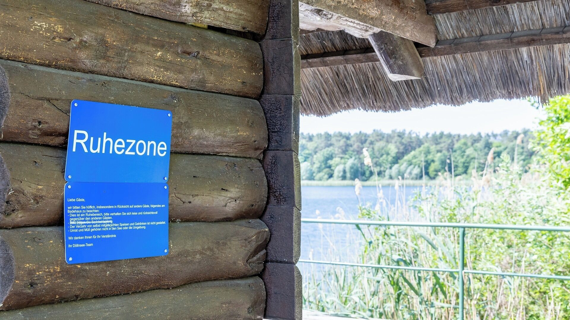 Uma cabana rústica com uma placa azul que diz 'Ruhezone' e vista para um lago.