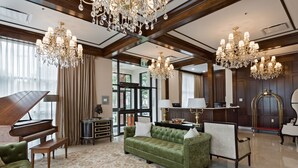 Um hall amplo com um piano de cauda, um sofá verde e várias luminárias de cristal.