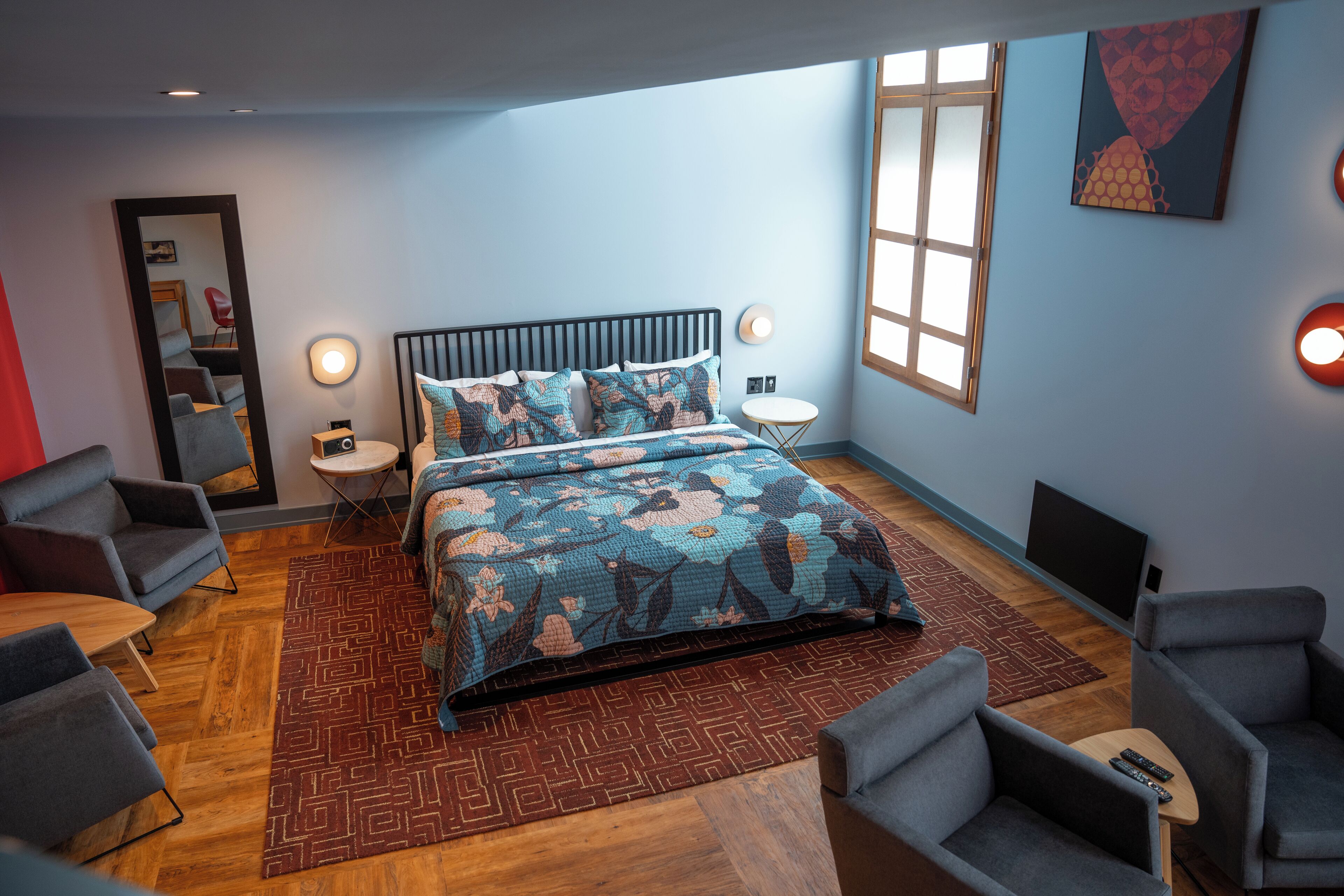 Quarto moderno com cama, mesas de cabeceira, espelho e janela.