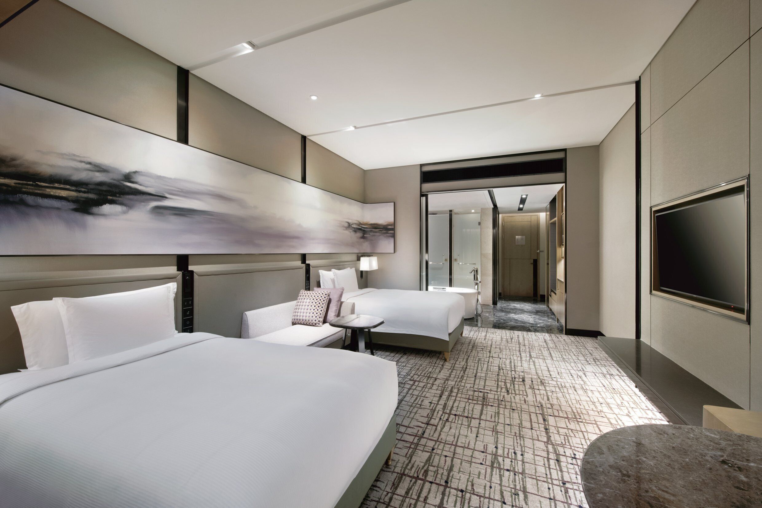 Quarto de hotel moderno com duas camas, área de estar, televisão e uma grande pintura abstrata na parede.