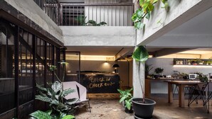 Espaçoso interior em estilo industrial, com balcão de recepção, plantas em vasos e área de cozinha.