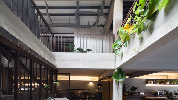 Um espaço amplo e interno com um mezanino, plantas em vasos e uma placa de check-in/check-out.