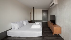 Quarto de hotel moderno com uma cama grande, um banco de madeira, uma televisão de tela plana e um ar condicionado.