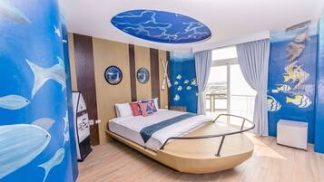 Quarto com cama curva, vista para o mar através de amplas janelas e um mural no teto com peixes.