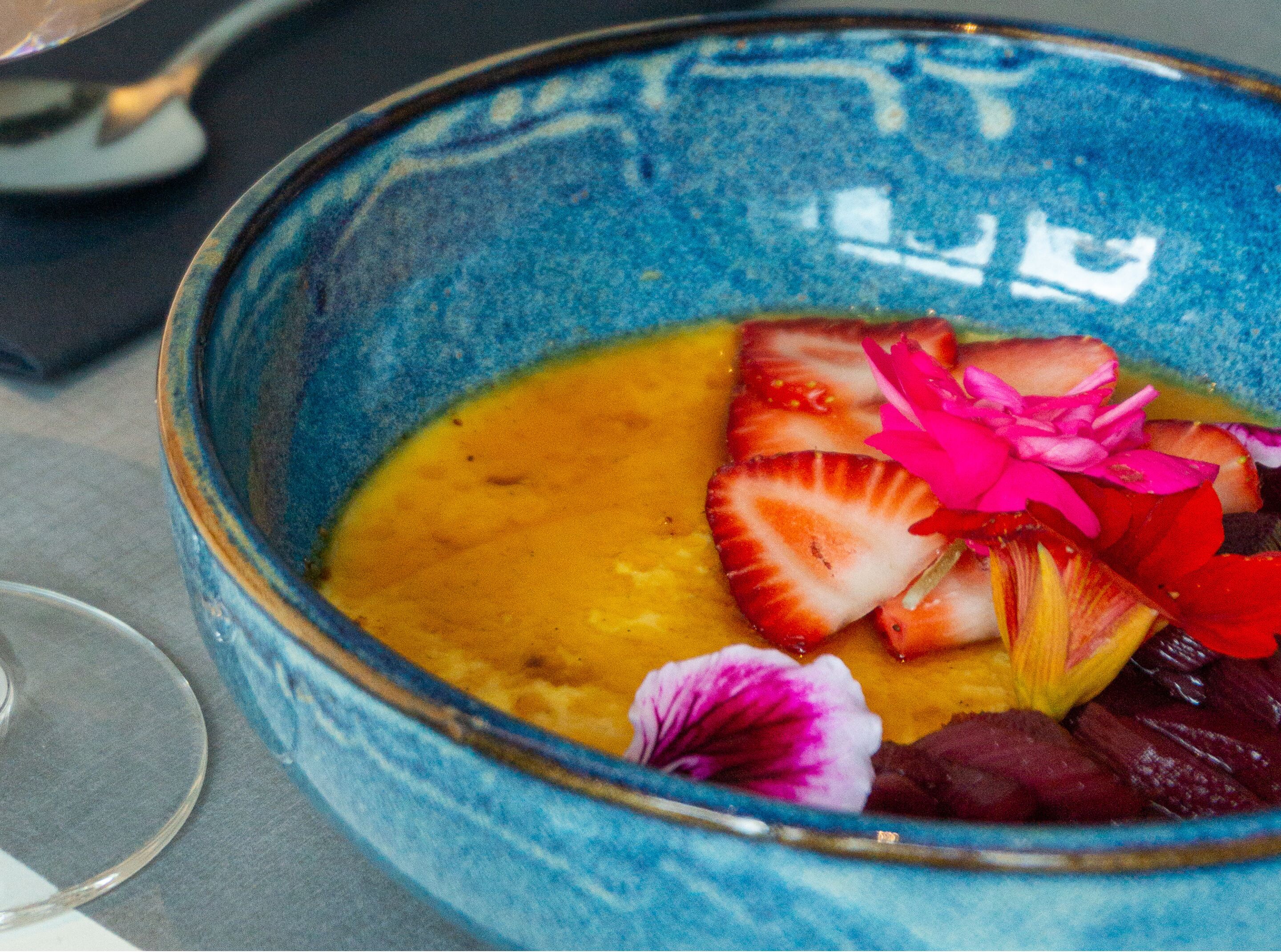 Uma tigela de sopa com morangos e flores.