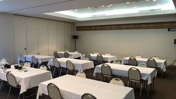 Sala de conferência com várias mesas e cadeiras, equipada com porta-nomes e computadores portáteis.