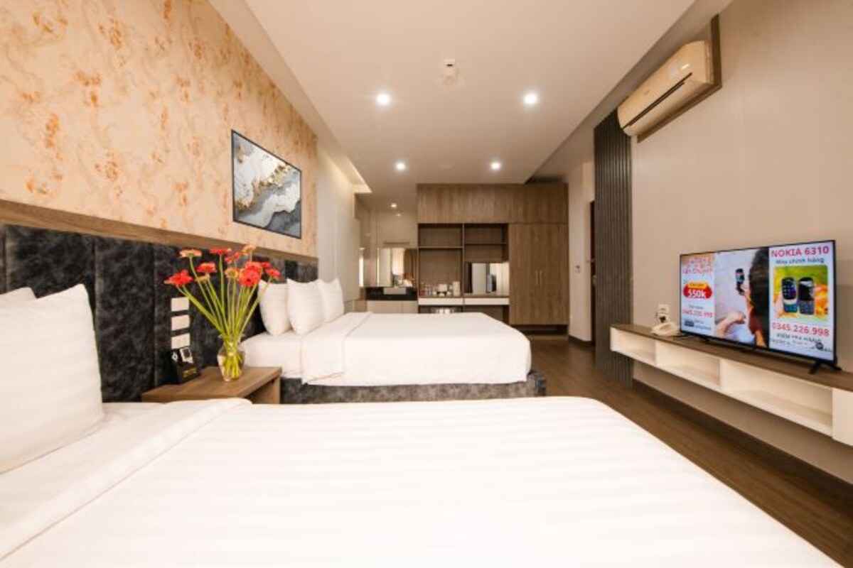 Quarto de hotel com duas camas, televisão, cozinha e banheiro.