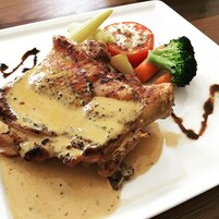 Um prato com um bife de porco grelhado, legumes e um molho cremoso.