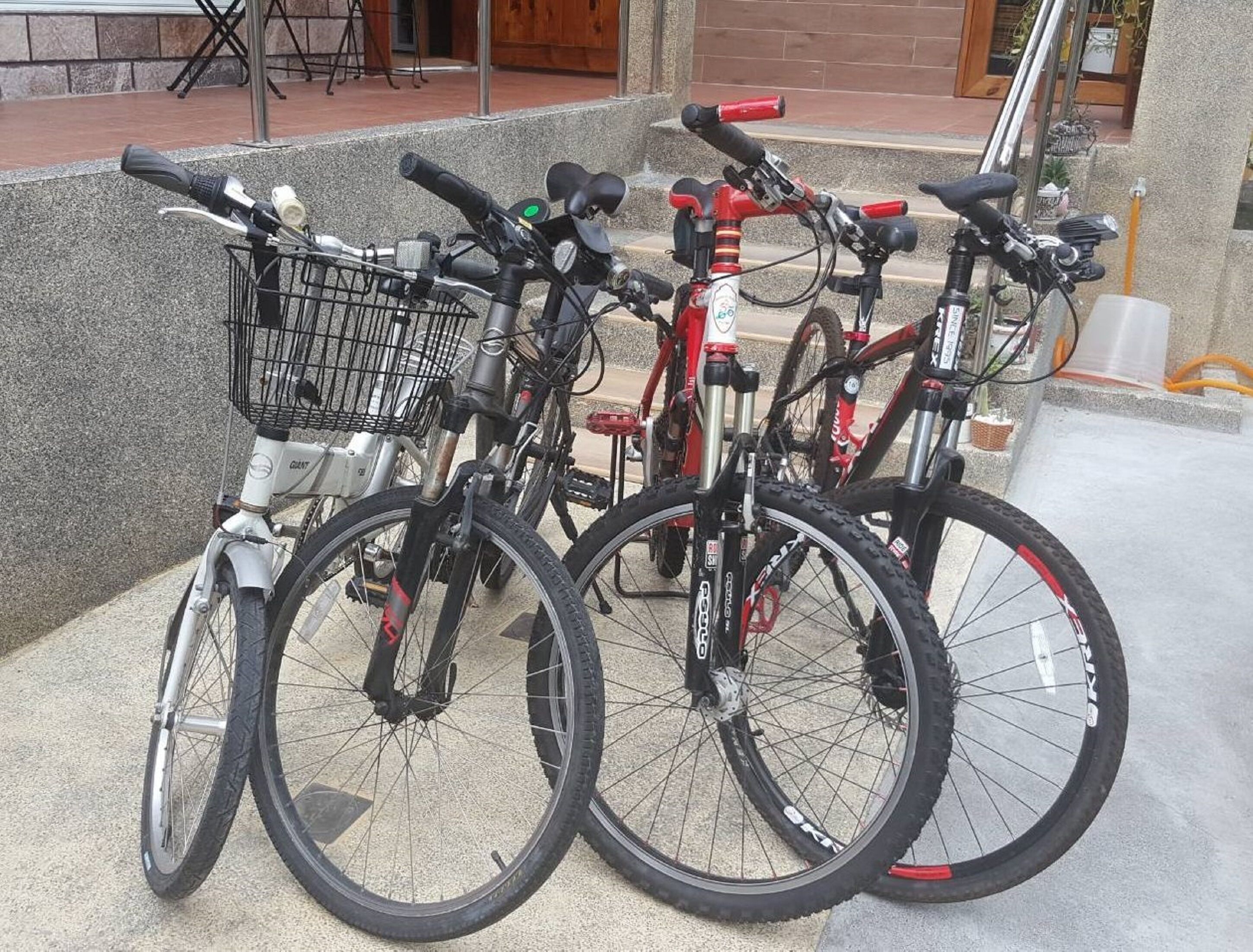 Três bicicletas estacionadas em uma superfície de concreto perto de uma entrada de edifício.