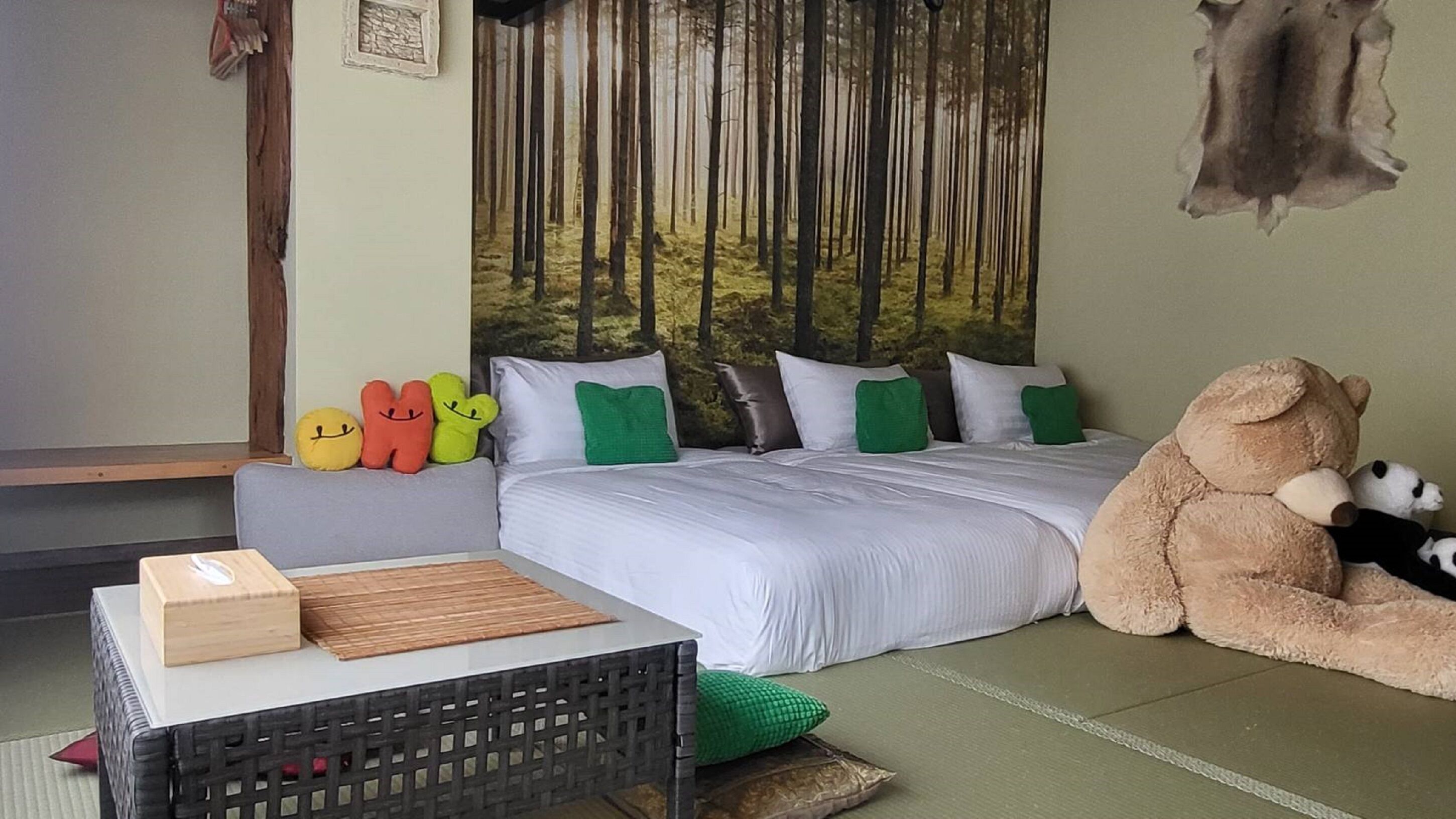 Quarto com cama, almofadas, um urso de pelúcia e um tapeçário na parede.