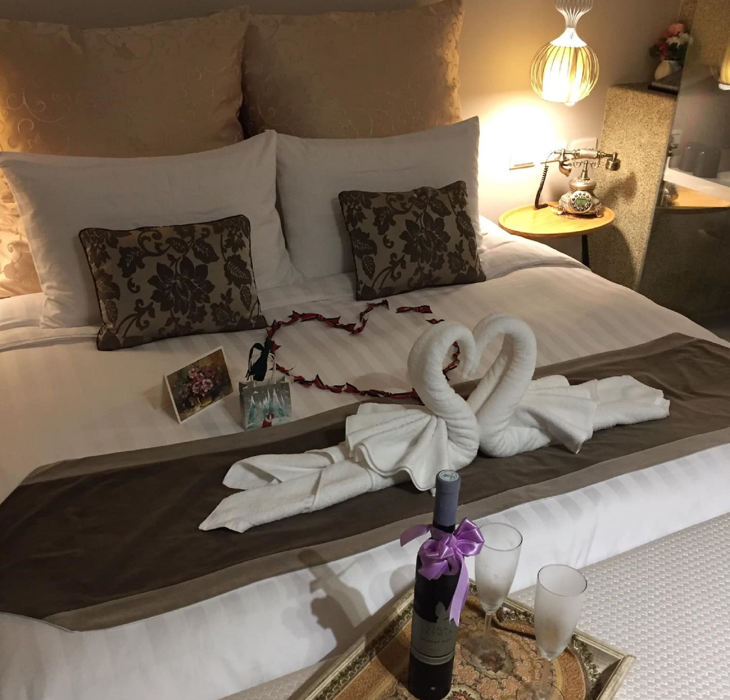 Cama arrumada com um arranjo de toalha em forma de cisne, uma garrafa de água e um copo sobre um tabuleiro.