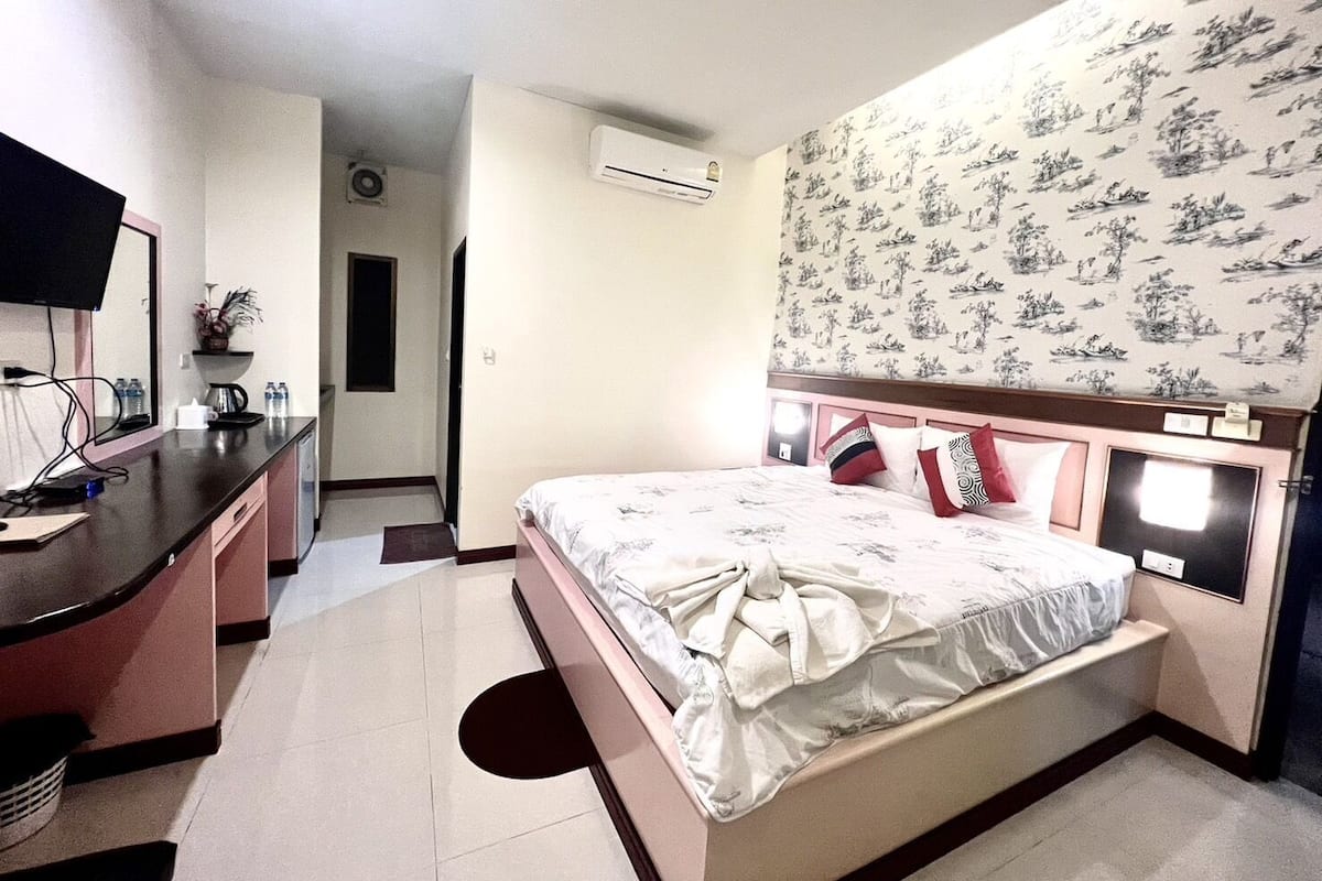 Quarto de hotel com cama, escrivaninha, televisão e ar condicionado, além de papel de parede estampado.