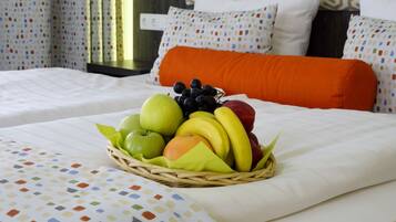 Cama arrumada com cesta de frutas sobre o lençol, almofada estampada e almofada lisa.