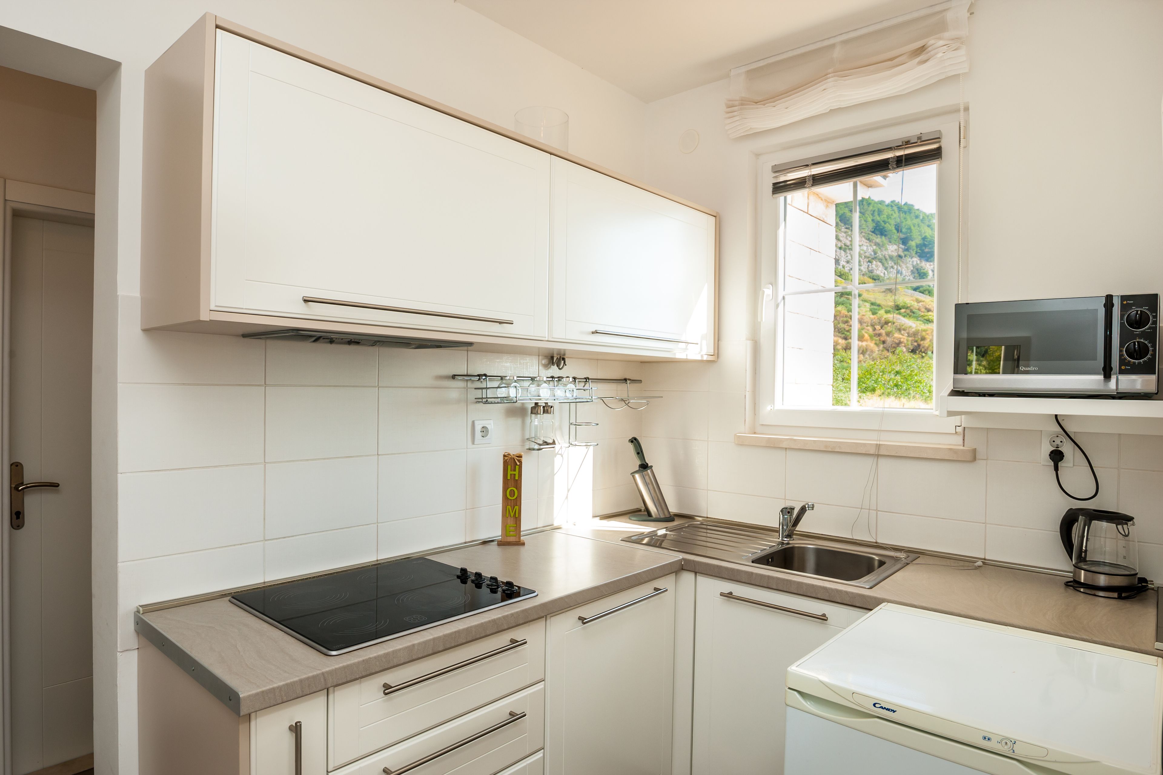 Uma cozinha moderna com armários brancos, micro-ondas embutido e janela com vista para o verde.