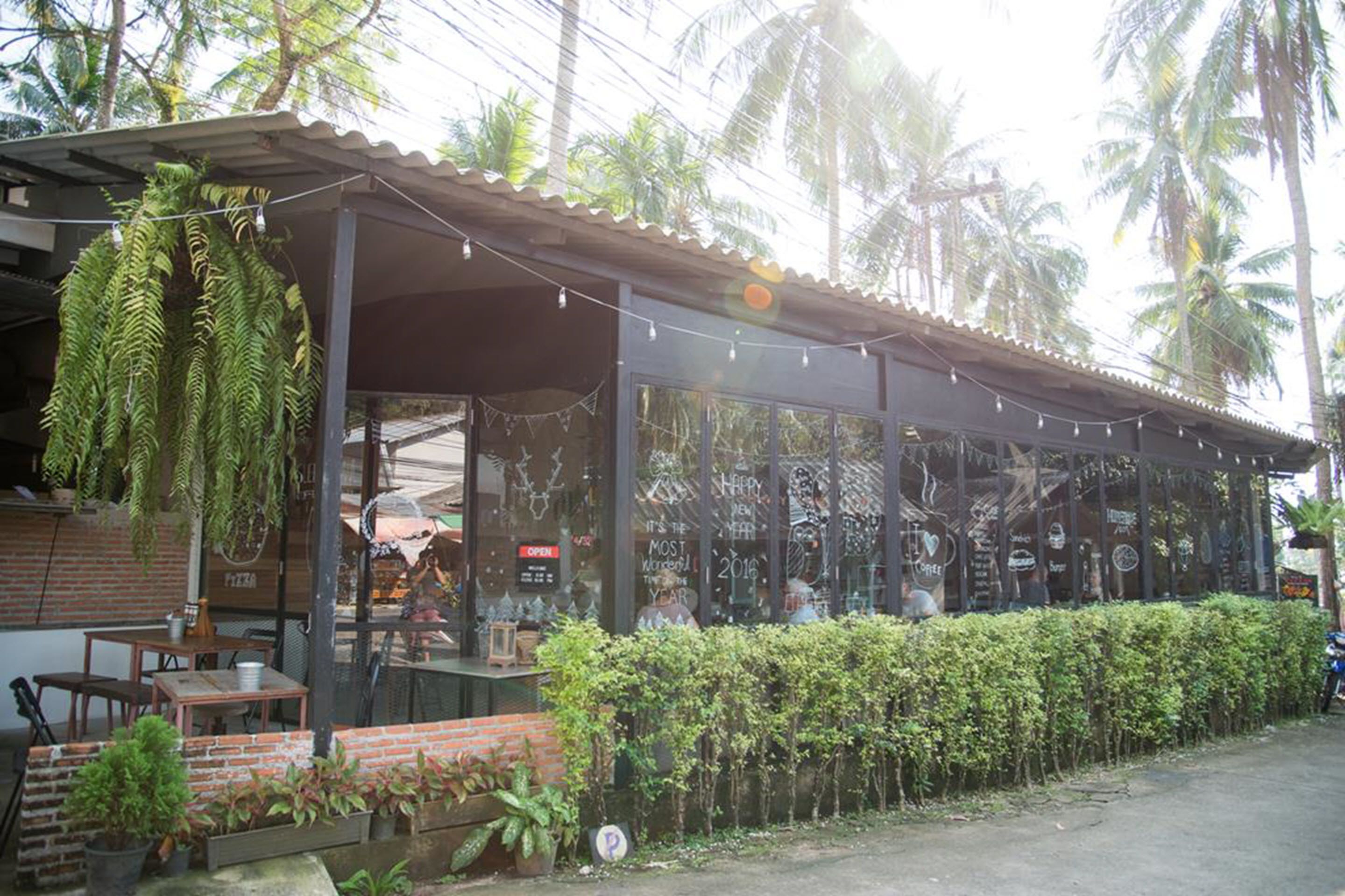 Um restaurante com área externa, um terraço coberto e vista para palmeiras.