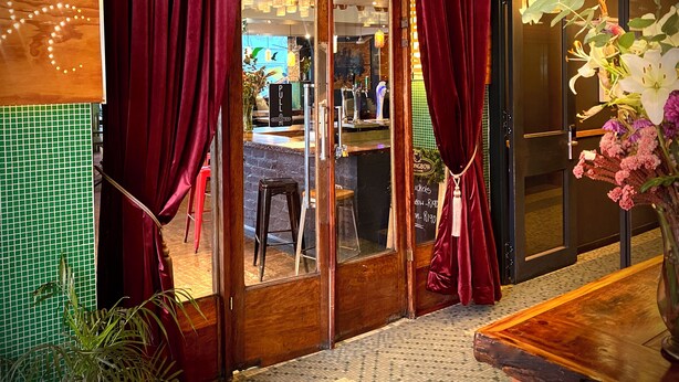 Entrada de hotel com porta de madeira, cortinas vermelhas, uma placa com a palavra