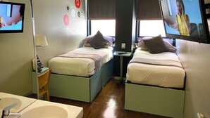 Quarto de hotel com duas camas, televisão, luminária e banheiro.