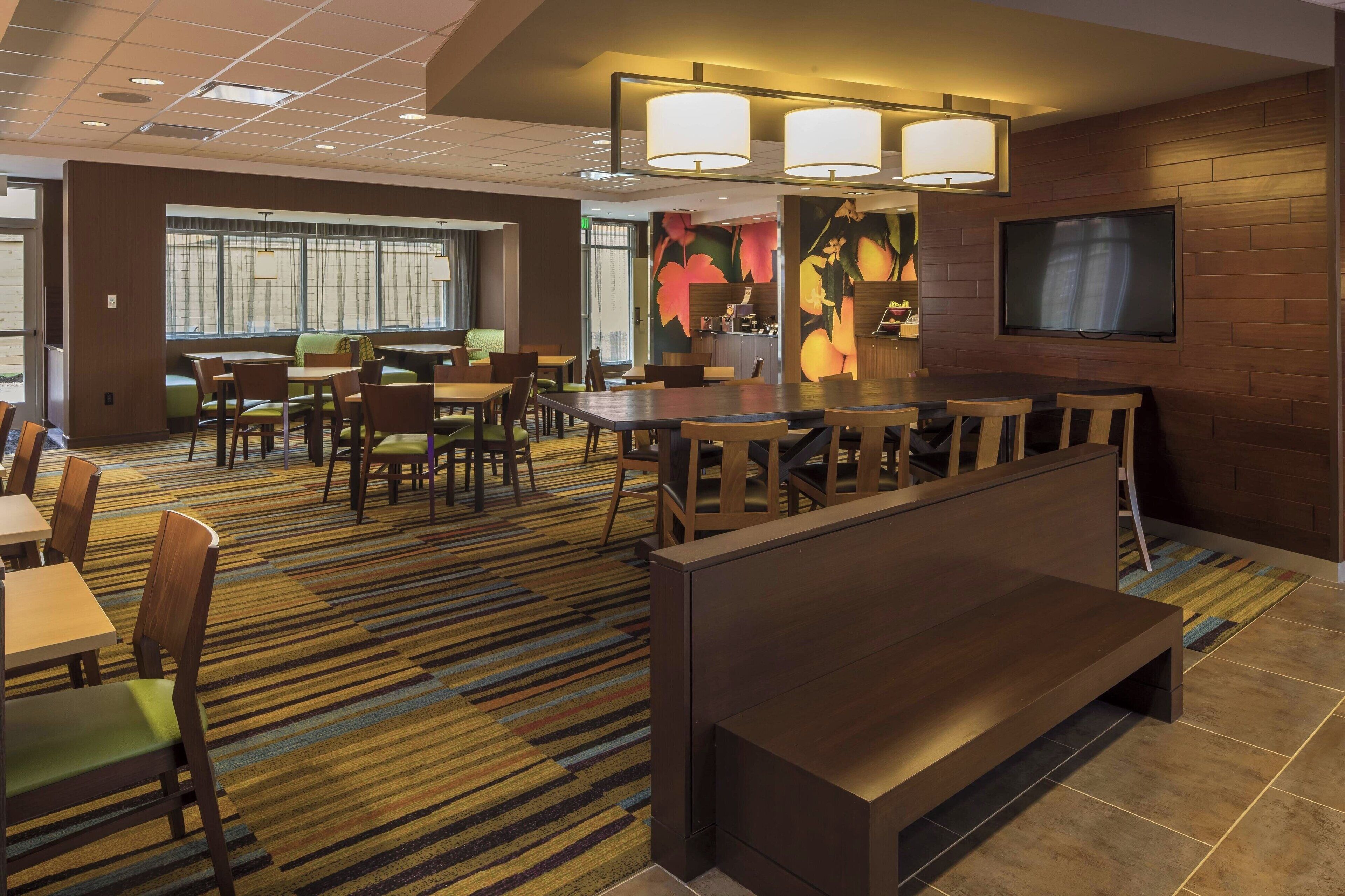 Um saguão de hotel com área de bar, assentos e uma tela de televisão.