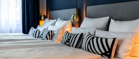 Quarto de hotel com uma cama grande, várias almofadas e cabeceira.