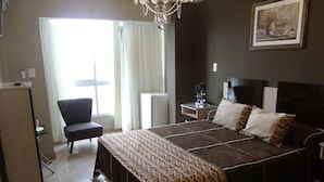 Quarto com uma cama grande, uma cadeira, escrivaninha e mesa de cabeceira.