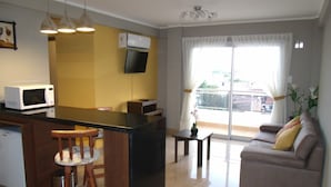 Um espaço compacto com cozinha compacta, sofá, mesa de jantar e televisão fixada na parede.