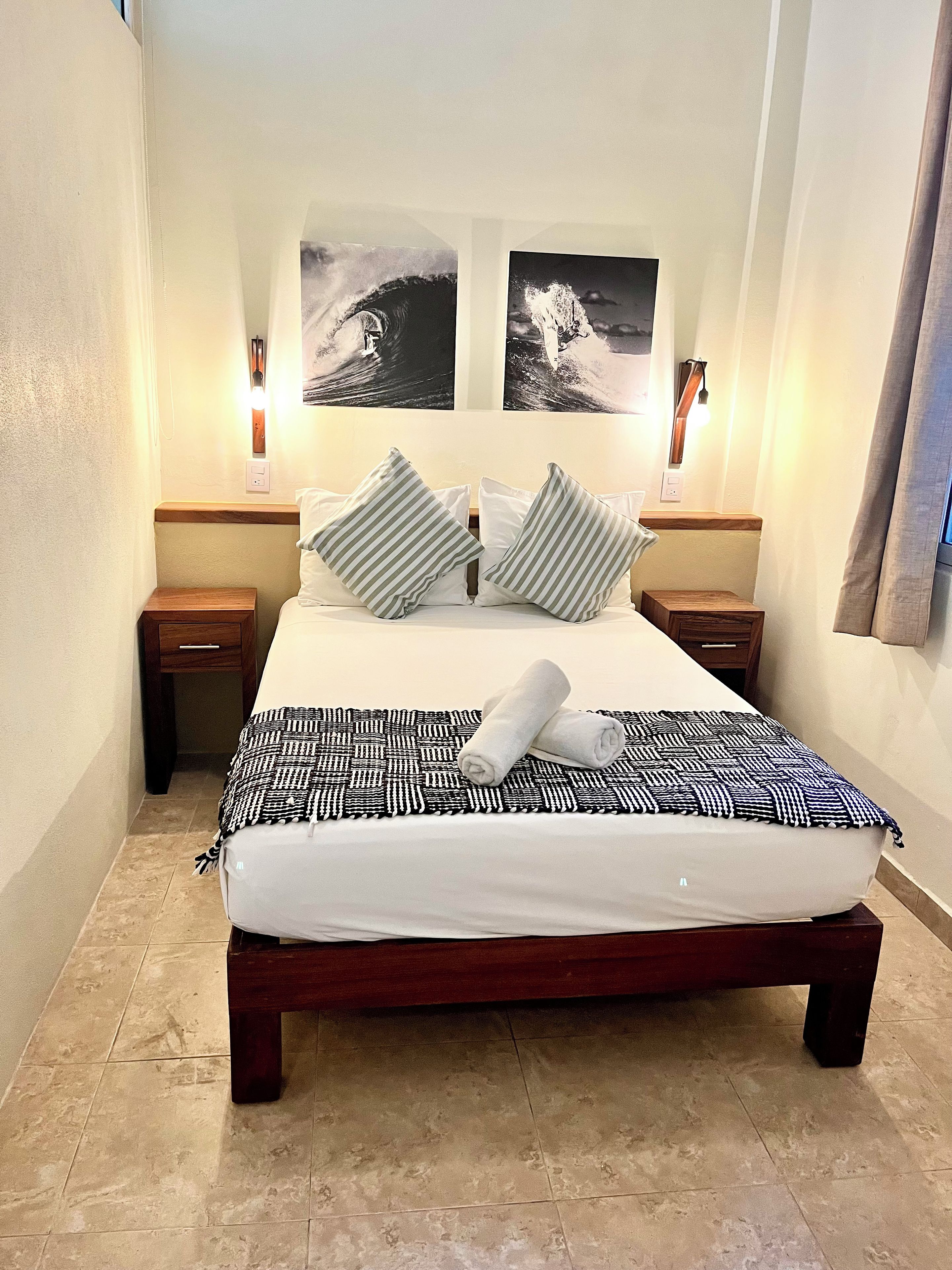 Quarto de hotel com cama, duas mesas de cabeceira, uma luminária na parede e duas fotos emolduradas.