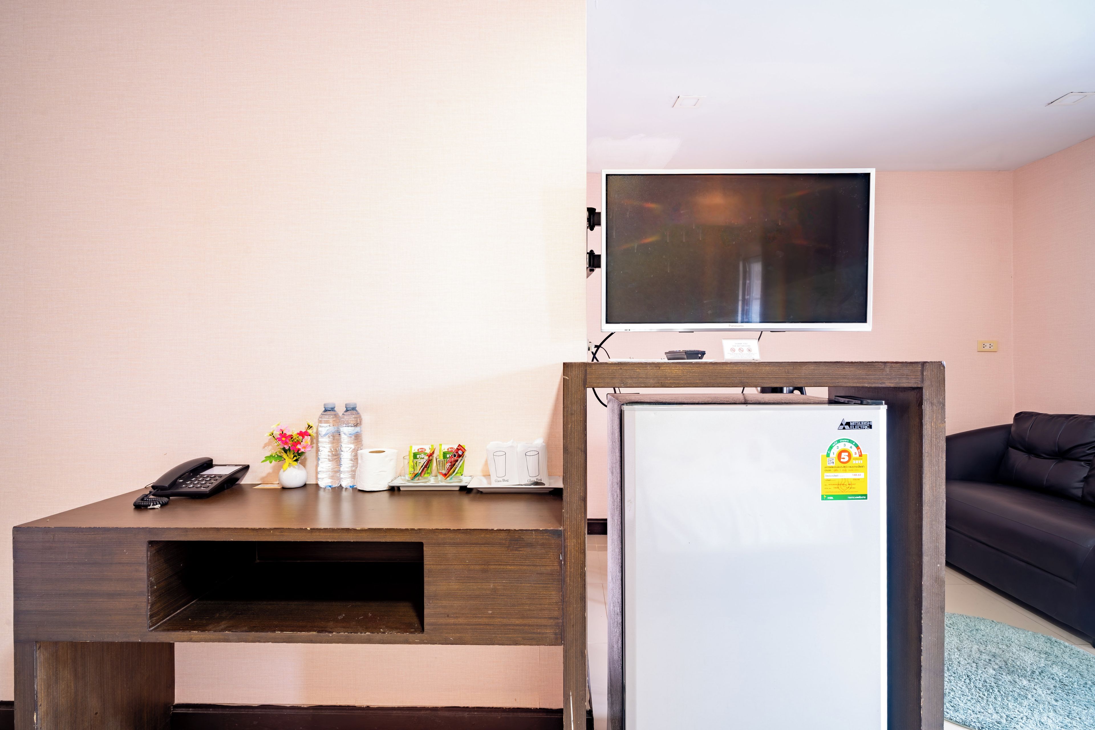 Quarto de hotel com escrivaninha de madeira, frigorífico, televisão na parede e sofá de couro preto.