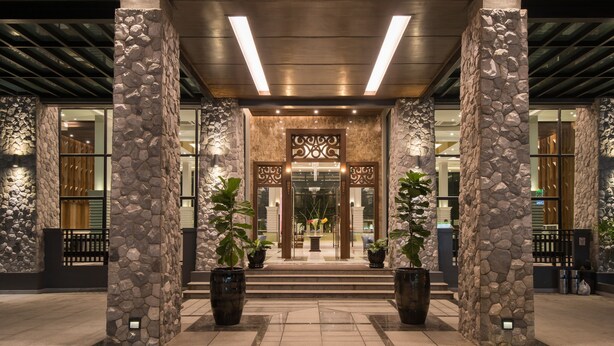 Entrada de hotel com pilares de pedra, teto de madeira e porta de vidro.