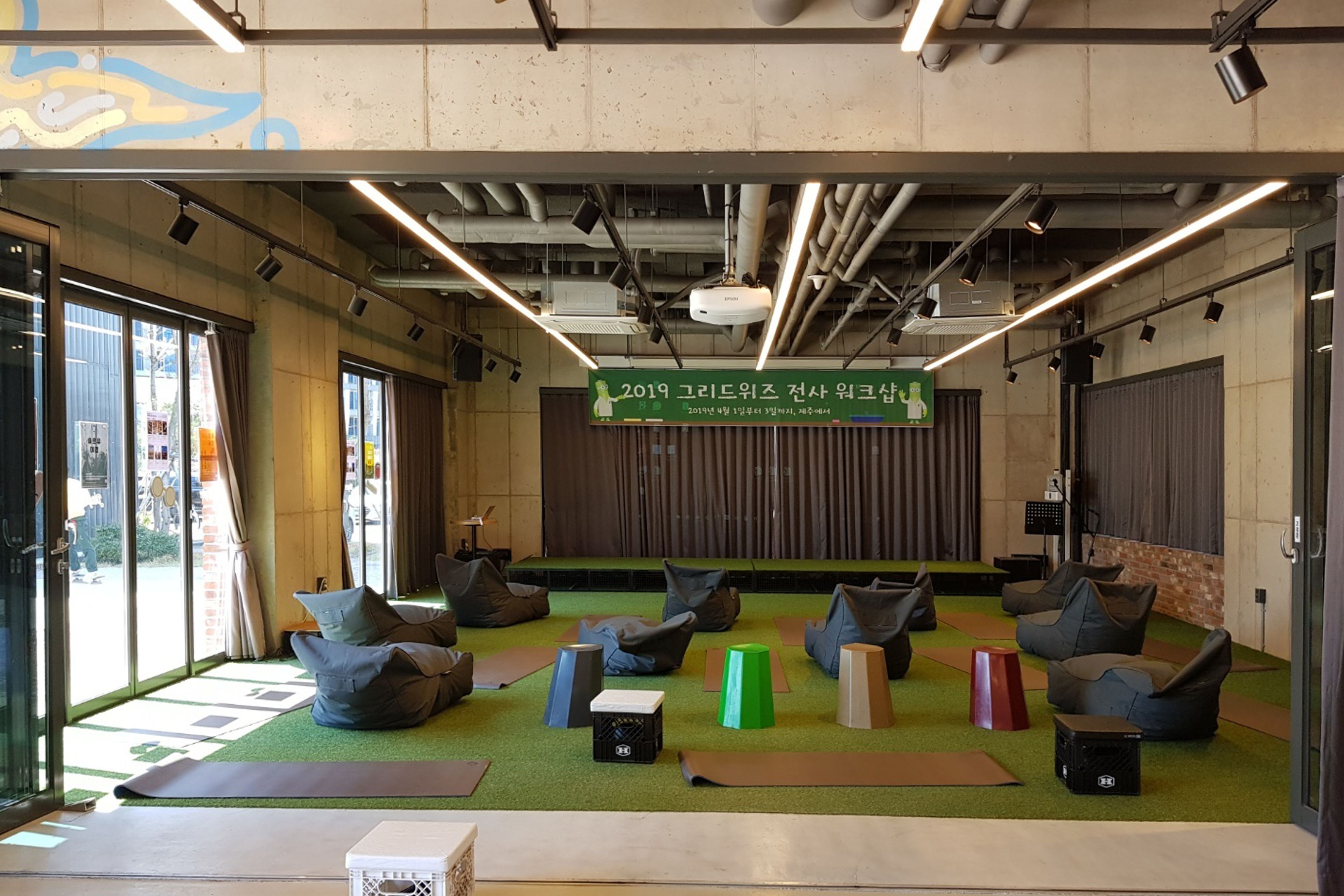 Quarto com puffs, tapetes e palco com um banner verde.
