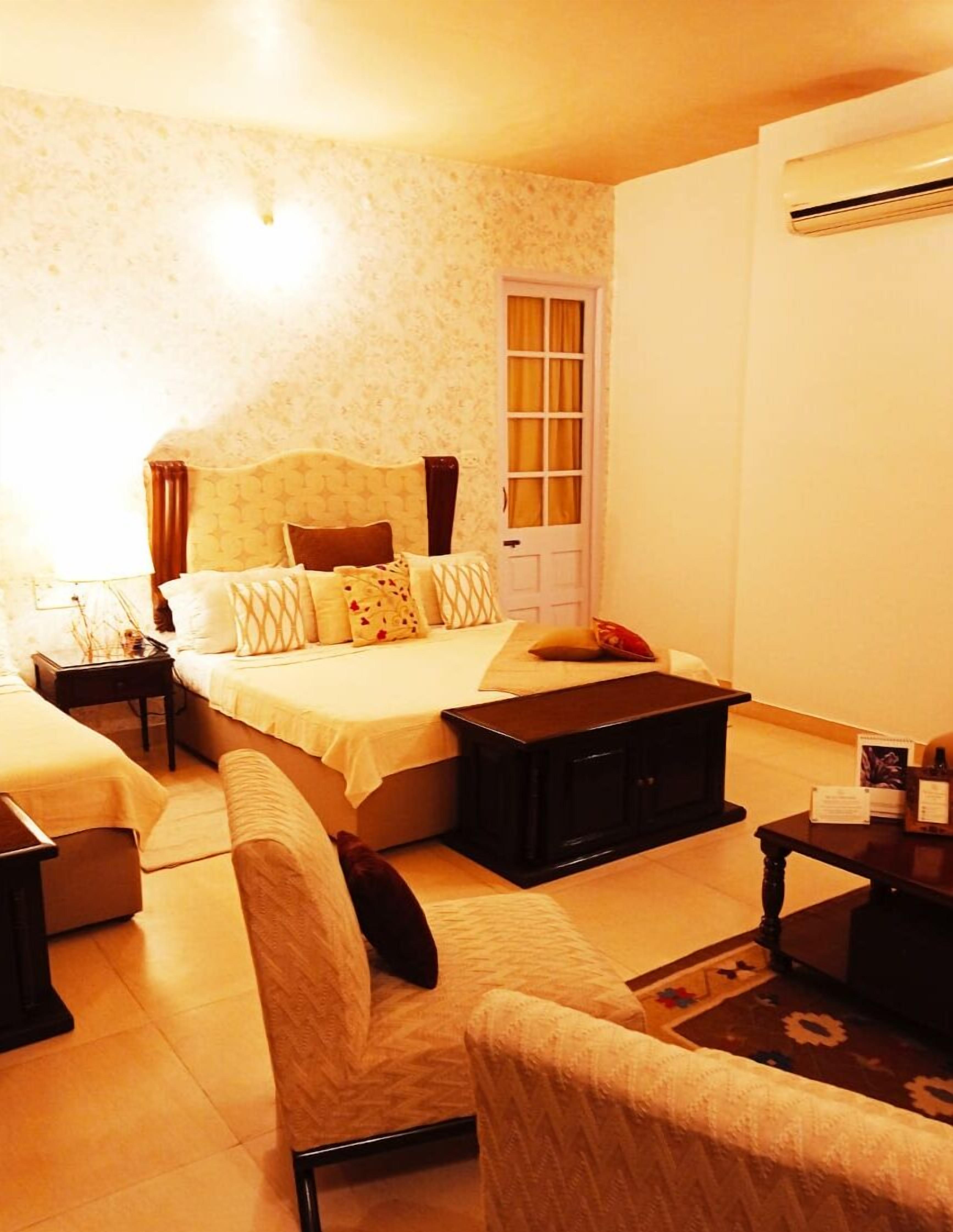 Quarto de hotel com cama, escrivaninha, cadeira e mesa pequena.