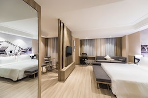 Quarto de hotel com uma cama grande, um sofá, uma escrivaninha com cadeira, uma televisão e um espelho.