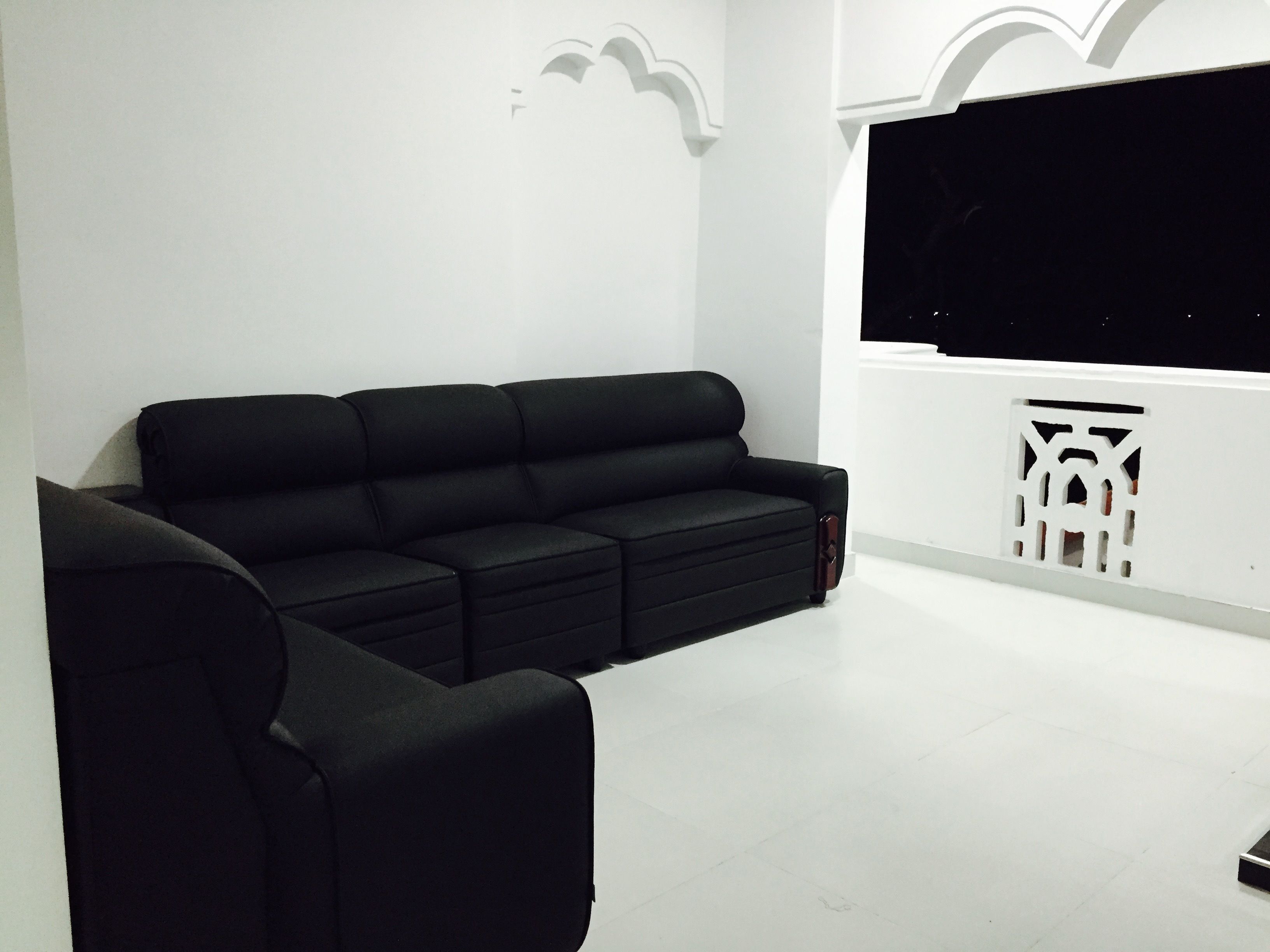 Uma sala de estar moderna com um sofá preto, uma TV de tela plana na parede e um painel branco decorativo abaixo da TV.
