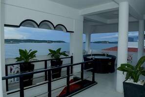 Varanda com vista para o mar, plantas em vasos e área de estar com mesa e cadeiras.