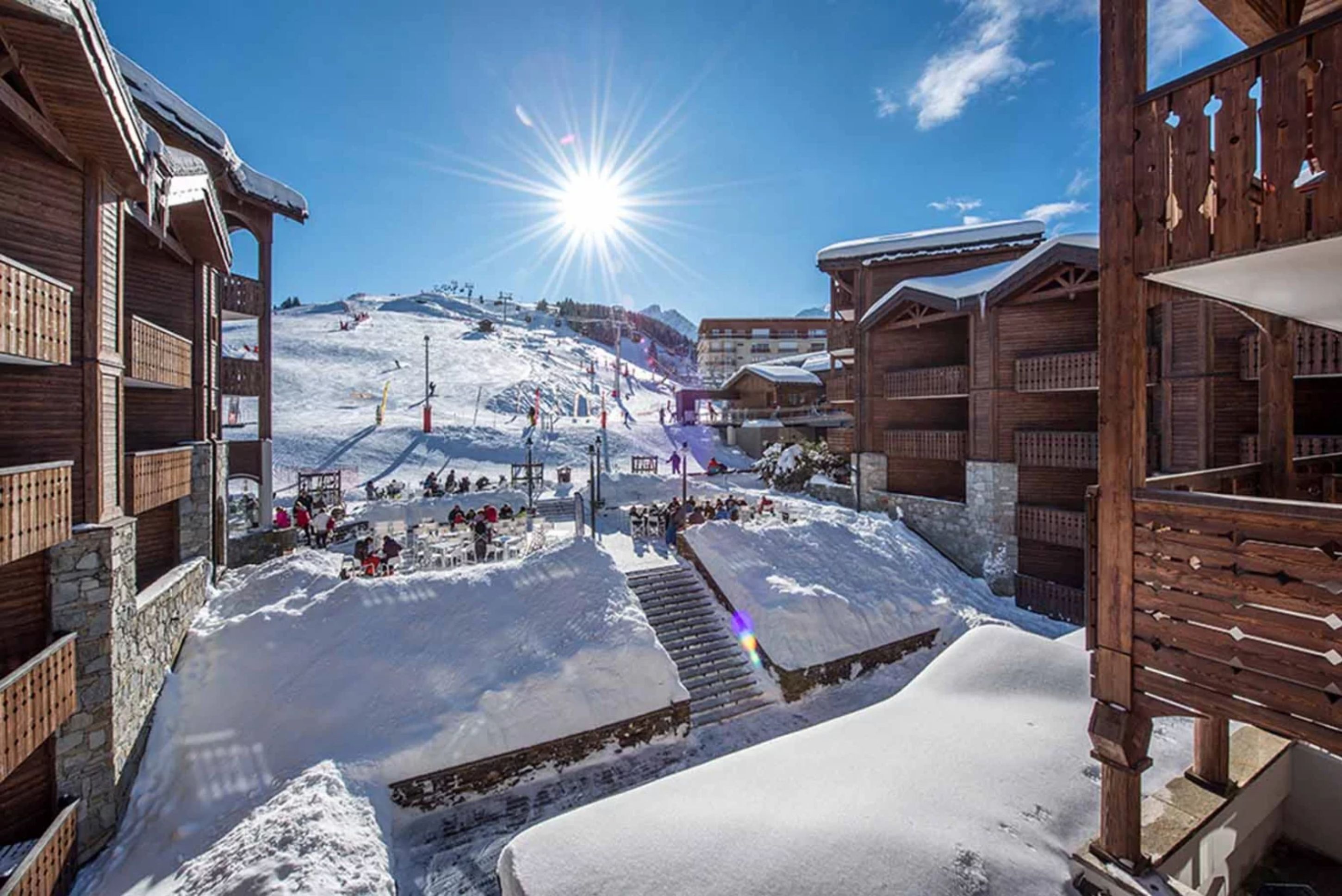 Estância de esqui coberta por neve, com edifícios de madeira e céu claro.