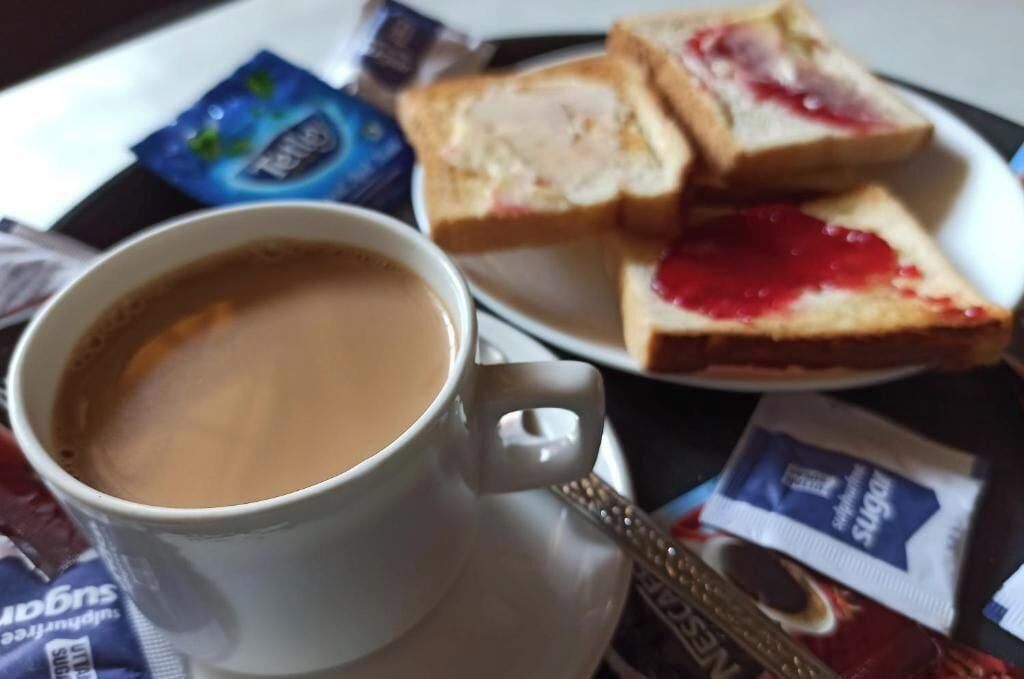 Uma chávena de café, um prato com duas fatias de tosta, e saquetas de açúcar e compota.