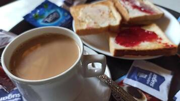 Uma chávena de café, um prato com duas fatias de tosta, e saquetas de açúcar e compota.