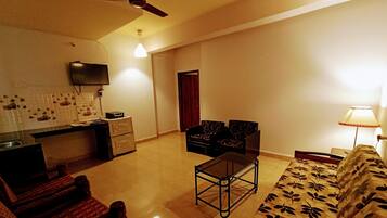 Uma sala de estar com sofá, mesa de centro, TV fixada na parede, ventilador de teto e abajur.