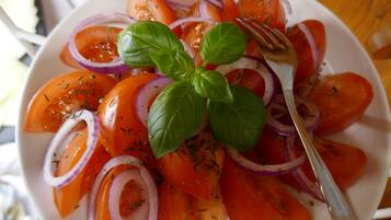 Um prato de tomates fatiados e cebola vermelha, decorado com folhas de manjericão.