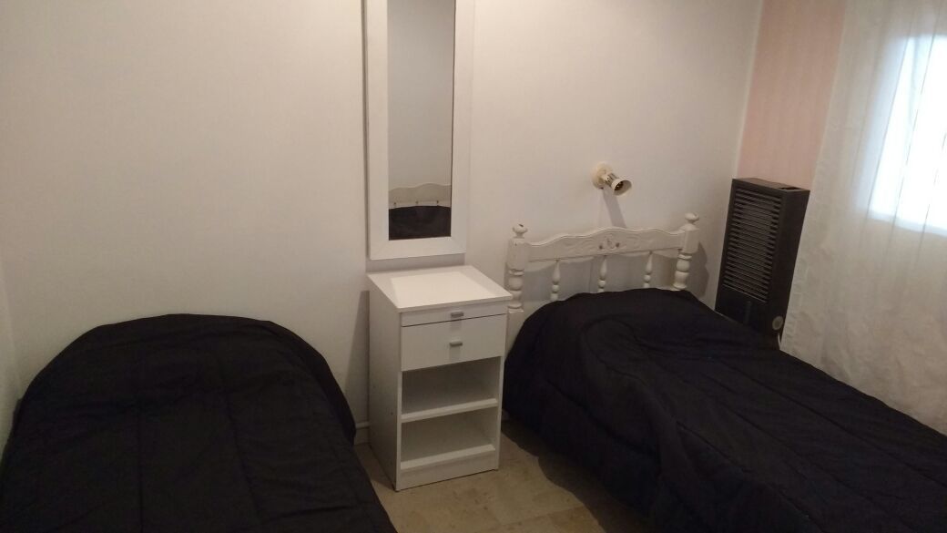 Quarto pequeno com duas camas de solteiro, cômoda branca com espelho e radiador.