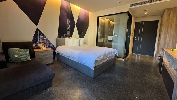 Quarto moderno com cama grande, área de estar, chuveiro em cabine de vidro e guarda-roupa em tons escuros.