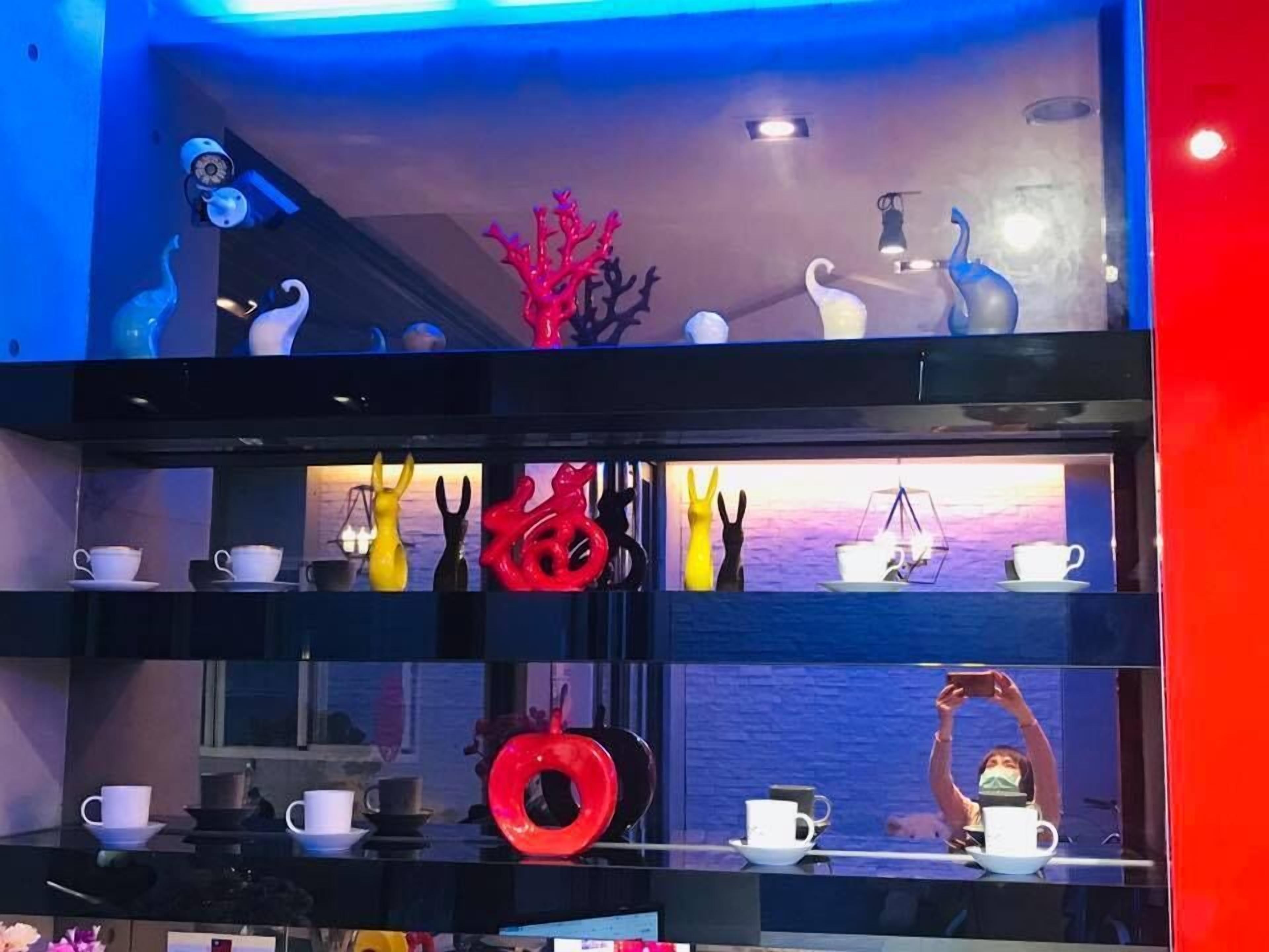 Um quarto com uma estante preta exibindo diversos objetos decorativos, incluindo xícaras e um objeto circular vermelho.
